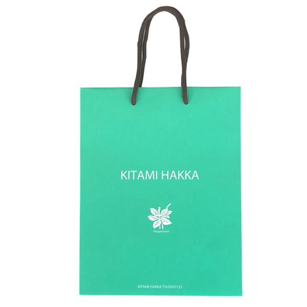 北見ハッカ通商オリジナルのギフト用手提げ紙バッグ。爽やかなペパーミントグリーンの表面と、清潔感のあるホワイトの裏面のコントラストが鮮やかで、中央に北見ハッカ通商のシンボルマークの「ハッカの葉」が配置されており、シンプルながら上品なデザインと...