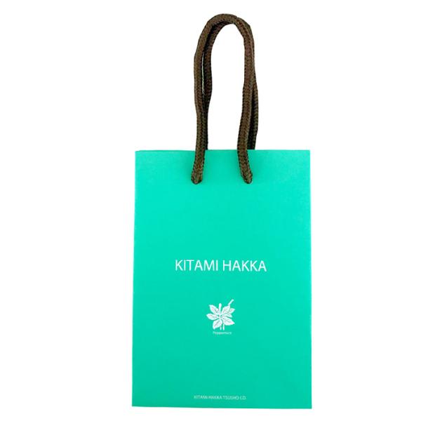 北見ハッカ通商オリジナルのギフト用手提げ紙バッグ。爽やかなペパーミントグリーンの表面と、清潔感のあるホワイトの裏面のコントラストが鮮やかで、中央に北見ハッカ通商のシンボルマークの「ハッカの葉」が配置されており、シンプルながら上品なデザインと...