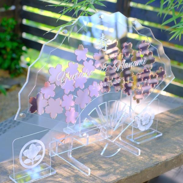 ミラーアクリルが綺麗な扇子型のウェディングドロップスです。縁起の良い扇子の形は和婚など結婚式のウェルカムスペース演出にぜひおすすめです。中に入れるピースはピンクゴールド色の桜型で上品な雰囲気です。扇子型ドロップスには新郎新婦様のお名前と挙式...
