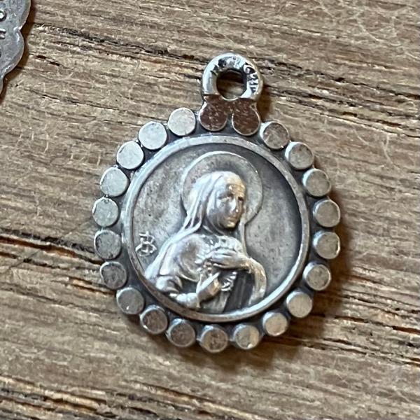 オランダ仕入れの品。1900年代中頃のものと思われる、巡礼用メダイです。胸元に十字架を抱く聖リタの肖像と、裏面には「STE RITA VENDEVILLE」の文字と、フランス・ヴァンデヴィルの聖リタ教会がかたどられています。丸カン部分に極小...