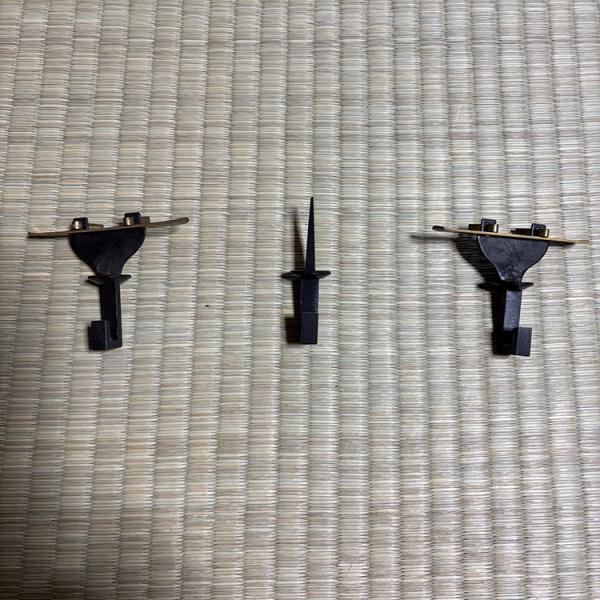 三福対は、床の間に掛軸や花入を美しく、安定して掛けるための伝統的な床の間用釘です。左右一対の受け金具と、中央の釘からなる三点構成により、掛物の重みを分散し、掛軸を正しく美しい姿で納めることができます。茶室や和室の床の間においては、掛軸は主景...