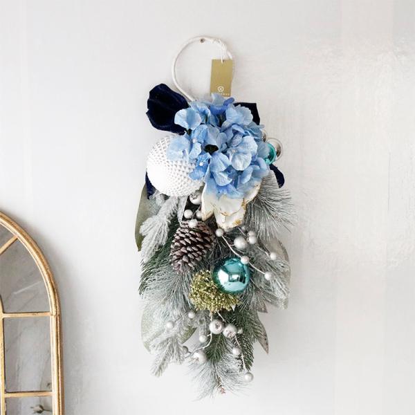 透明感のあるブルーの花と、輝くシルバーオーナメントが美しく調和したクリスマススワッグ。柔らかな雪をまとったような針葉や松ぼっくりが、季節のぬくもり感じさせる上質なデコレーションです。サイズ(約)幅27×高さ60cm材質/PVC,プラスチック...