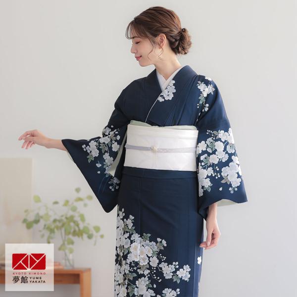 優雅な野ばらが咲き誇る訪問着。紺色に、やさしく流れる流水文様と、白の野ばらが舞うように描かれた一着。肩から袖、裾へと流れるような柄付けが、まるで風にたなびくような軽やかさを演出し、立ち姿まで美しく見せてくれます。さらに、一部にあしらわれた刺...